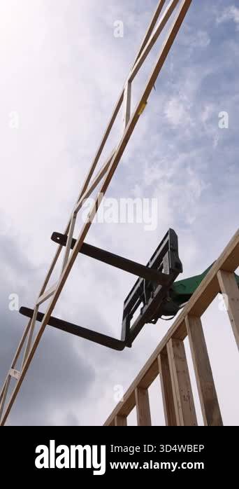 Workers use telehandler lift to position wooden truss in building under ...