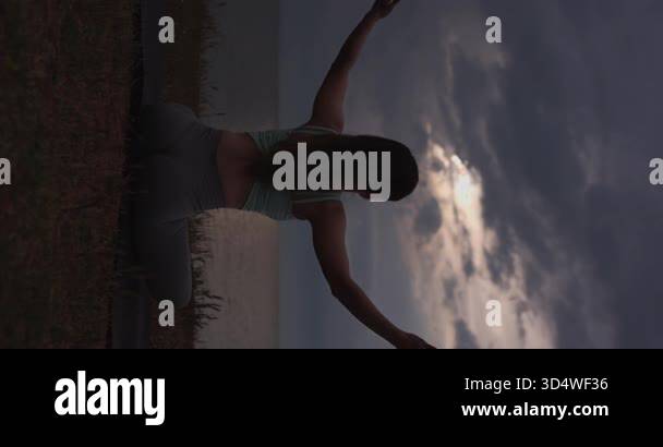 Woman doing yoga exercises on a hill against sea and sunset background ...