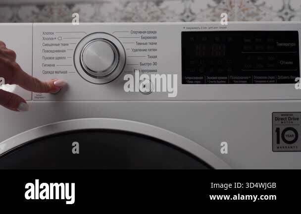 Close-up of a womans hand operating a modern washing machine, pressing ...