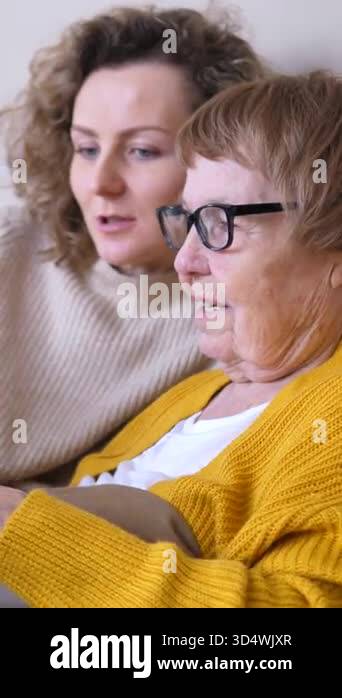 Young woman showing her grandmother how to use a laptop. Helping the elderly person learn new ...