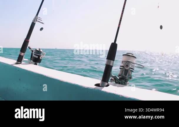 Two fishing rods in holders on a boat overlook a turquoise sea ...
