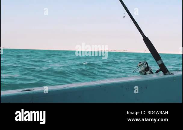 A fishing rod and reel in a holder on the side of a boat The boat moves ...