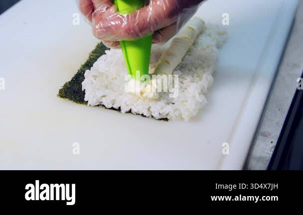 Gloved hands using green piping bag to add creamy filling to sushi rice ...
