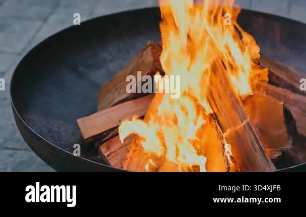 roaring orange flame in metal bowl, stacked wood logs ignite with ...
