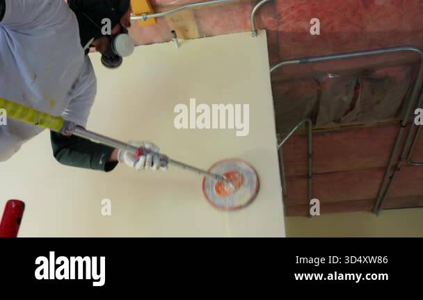 Construction worker is sanding a drywall surface using electric drywall ...