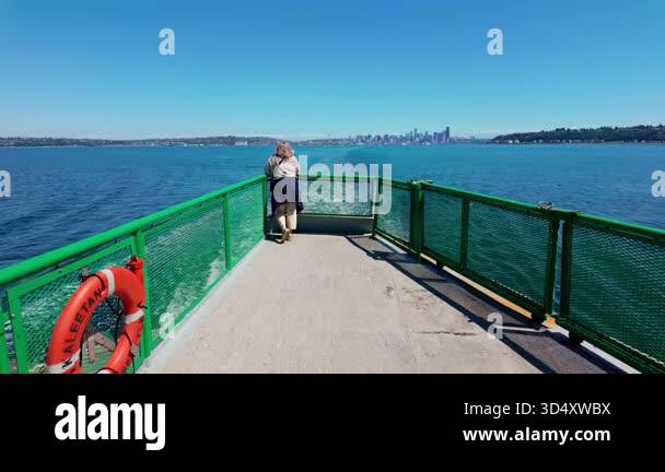 Passenger stand on the open deck of a Seattle ferry. Green railings and ...