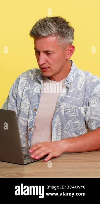 Middle-aged man focused while typing on laptop at table, showing ...