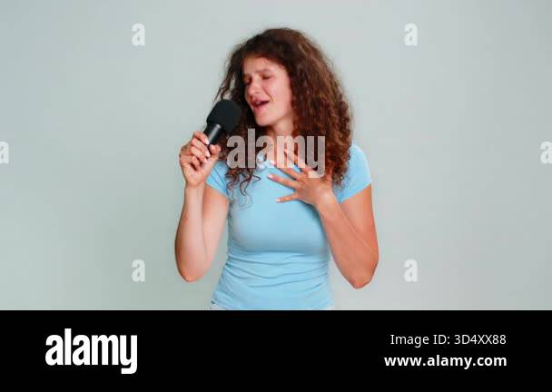 Young woman enthusiastically singing into microphone performing ...