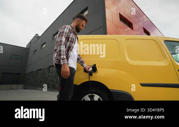 Young man unplugging the charging cable from his yellow electric van ...