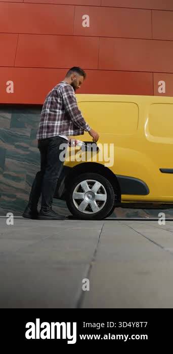 Young man unplugging a charging cable from a yellow electric commercial ...