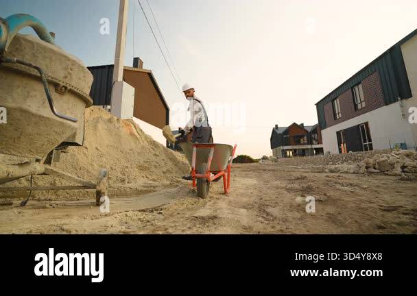 Male construction worker in a hard hat shoveling sand from a large pile ...