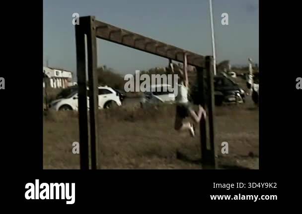 Young girl on monkey bars with parked cars behind in nostalgic frame ...