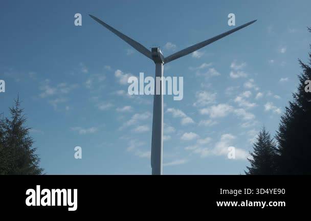 A large wind turbine stands tall, its blades slowly turning against the ...