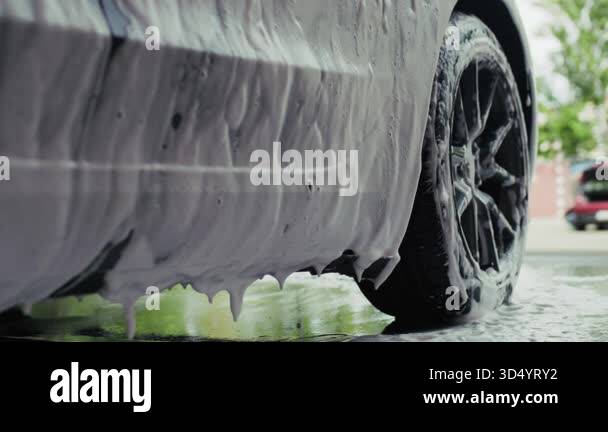 A car stands at the car wash fully covered in foam, with thick white ...