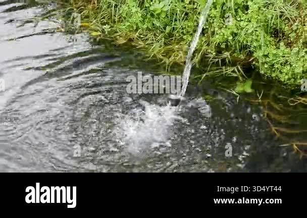 A clean 4K handheld shot of water splashing from a pipe into a small ...
