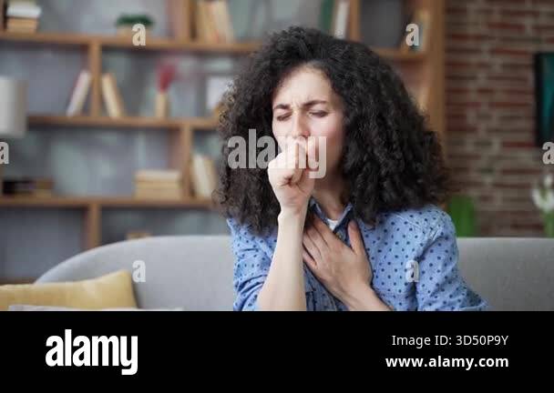 Sick young woman coughing while sitting on sofa in living room at home ...
