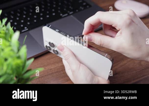 Close-up of a hand inserting a SIM card tray into a white smartphone ...