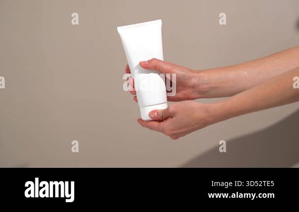 Young woman's hand open white mockup tube of cream and squeeze it into ...