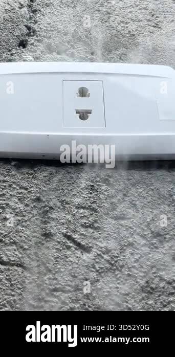 A smoking electrical outlet on a gray concrete wall from overvoltage ...