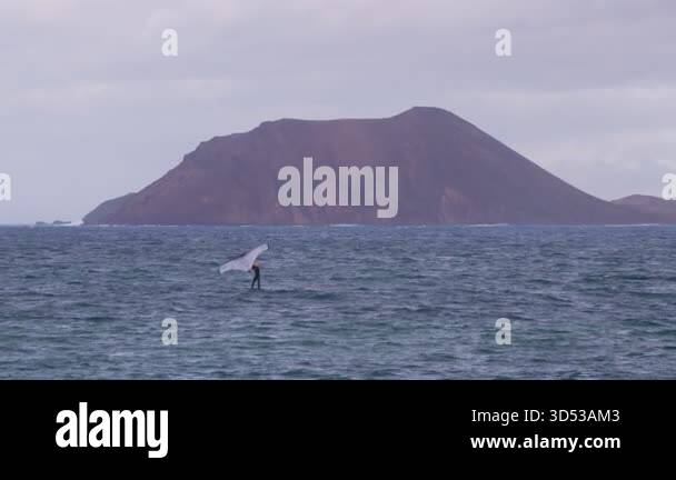 A windsurfer glides across calm waters near a stunning island ...