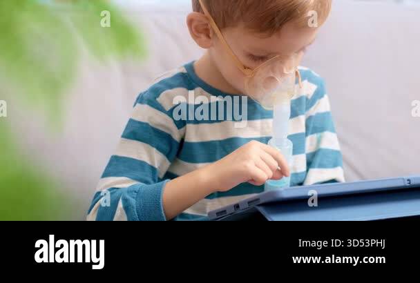 A young boy uses a nebulizer for respiratory treatment while ...