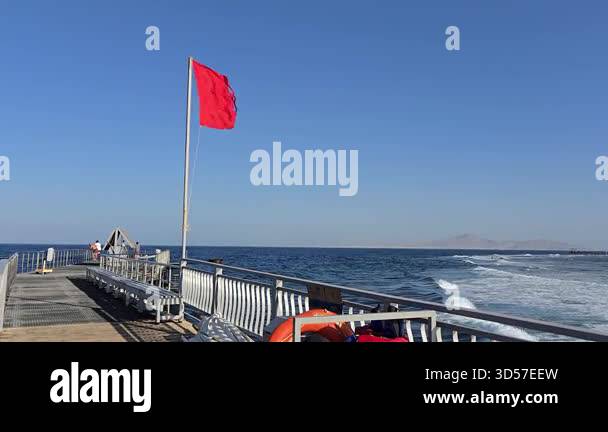 A red flag flutters in the wind on a pontoon by the sea. A strong wind ...