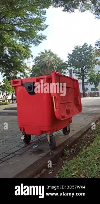 A bright red trash bin standing neatly in a city park, surrounded by ...