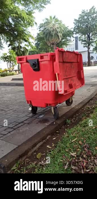A bright red trash bin standing neatly in a city park, surrounded by ...
