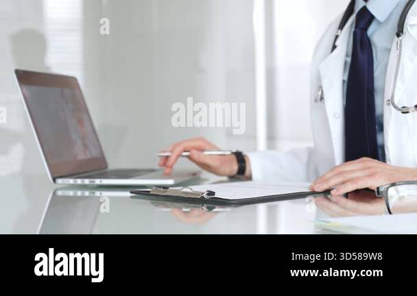 Doctor writing notes on clipboard while consulting a patient in a light ...