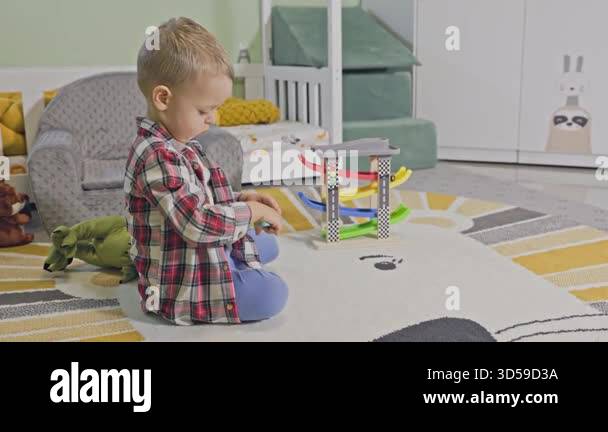 Adorable toddler sitting on a rug and playing with a colorful wooden ...