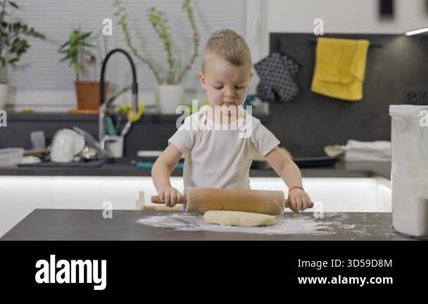 Cute toddler with flour on his face is learning how to bake, using a rolling pin on dough Stock ...