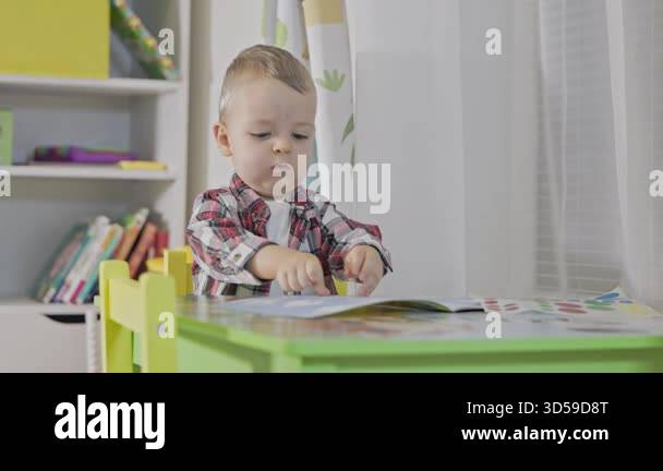Concentrated little boy sitting at a table applying stickers to a book ...