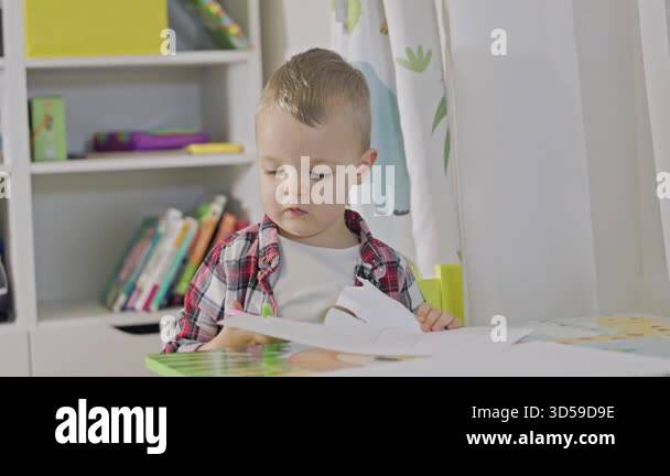 Cute toddler boy cutting paper with scissors at the table, developing ...