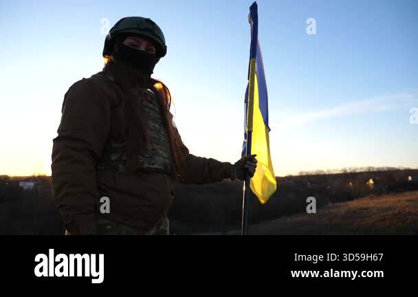 Woman in military uniform stands against sunset and lifted up flag of ...