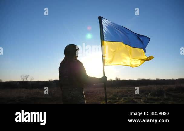 Female ukrainian army soldier holding waving flag of Ukraine with sun ...
