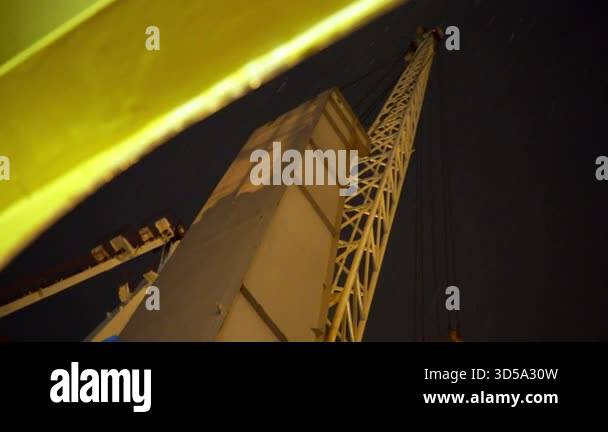 Rain streams down colossal crane tower glowing in harsh light ...
