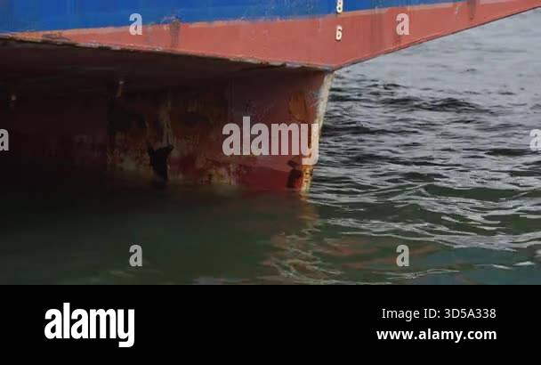 Steel hull of vessel rests in calm water with gleaming faintly draft ...