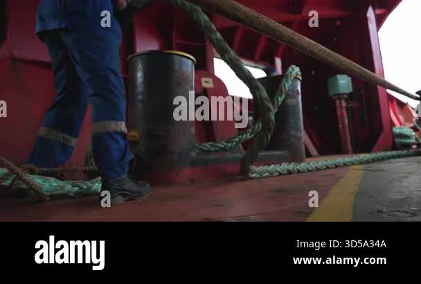 Skilled worker in uniform unties cable from metal supports in vessel ...