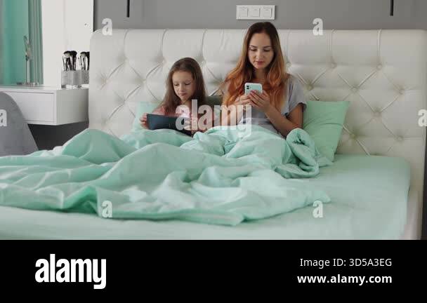 Mom and her little daughter, both in pajamas, are sitting in bed after ...