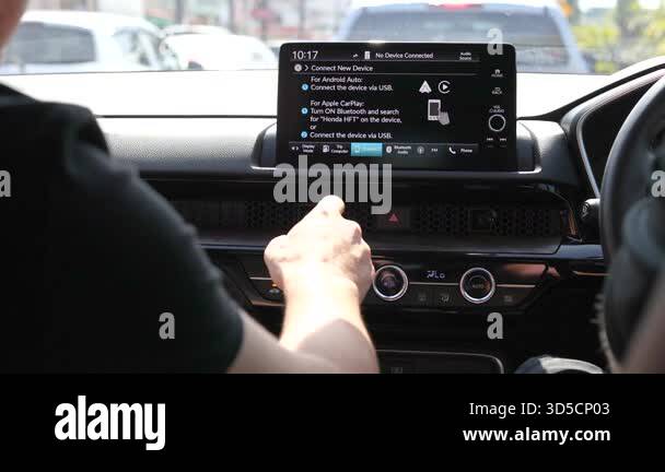 A driver operates a car's touchscreen console in daylight, adjusting ...