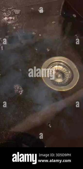 Rinsing and washing dishes under running water in black kitchen sink ...
