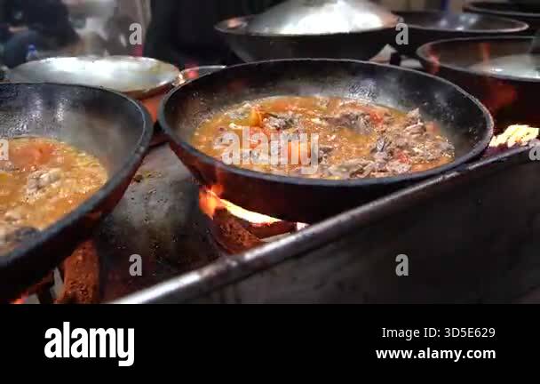 Cooking Scene Two black pans bubble with a tomato based meat stew ...