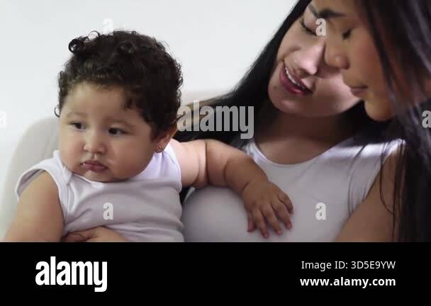 Tender moment as Latina moms hold their baby girl on their laps in a ...