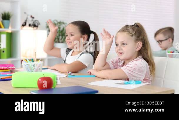 Smiling little girls raising hands at wooden desk during lesson in ...