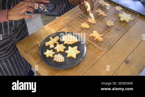 Diverse couple piping icing cookies while capturing smartphone photos ...