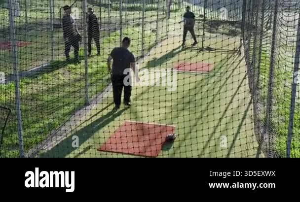 White male batter swinging bat in batting cage as pitcher winding arm ...