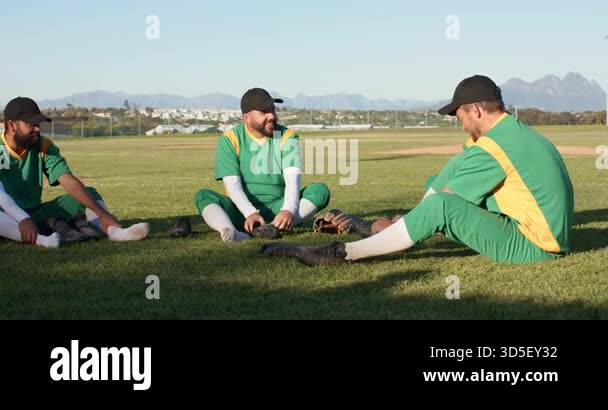 Stretching legs and adjusting cleats, diverse male baseball teammates ...