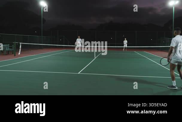 Bouncing neon yellow ball, male tennis player serving on floodlit court ...