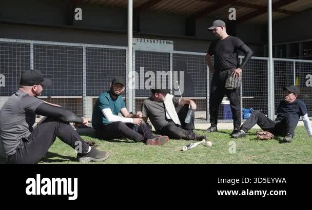 Diverse male baseball teammates passing water bottle and inspecting ...