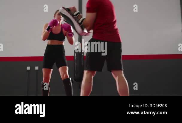 With coach holding pads, female boxer trainee launching kicks and ...